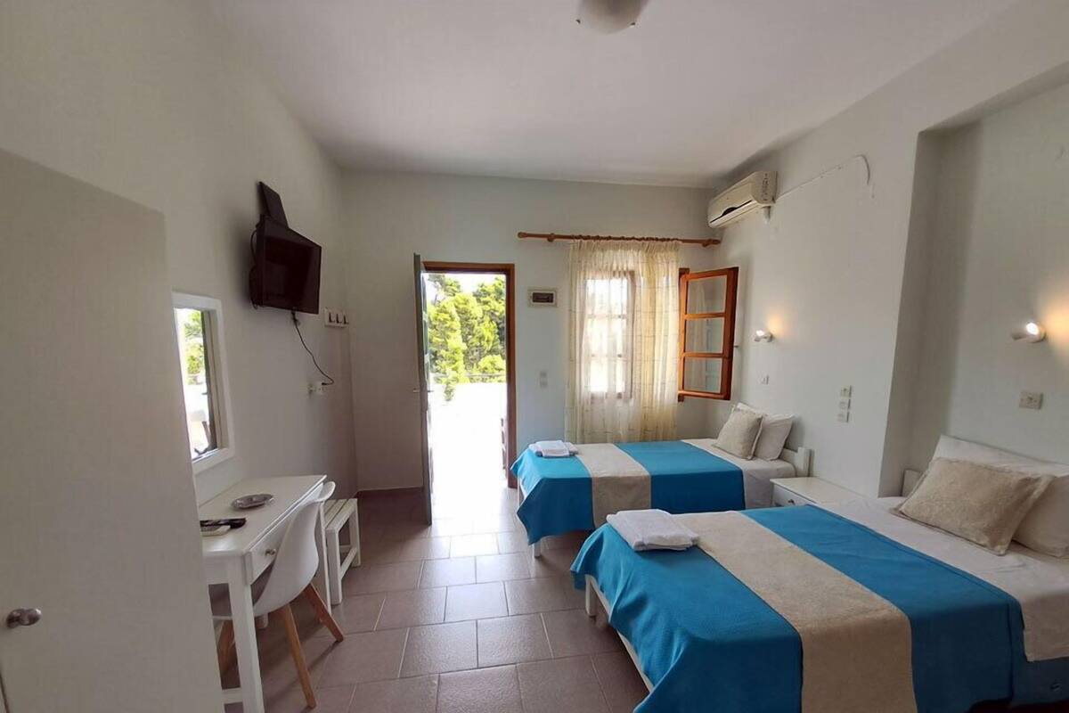 Quarto de hotel com duas camas, uma escrivaninha, uma televisão e uma janela com cortinas.