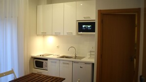 Uma cozinha compacta com armários brancos, micro-ondas, pia e um pequeno frigorífico.