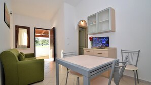 Um espaço de estar compacto com um sofá verde, uma mesa de jantar com cadeiras, uma televisão e um armário.
