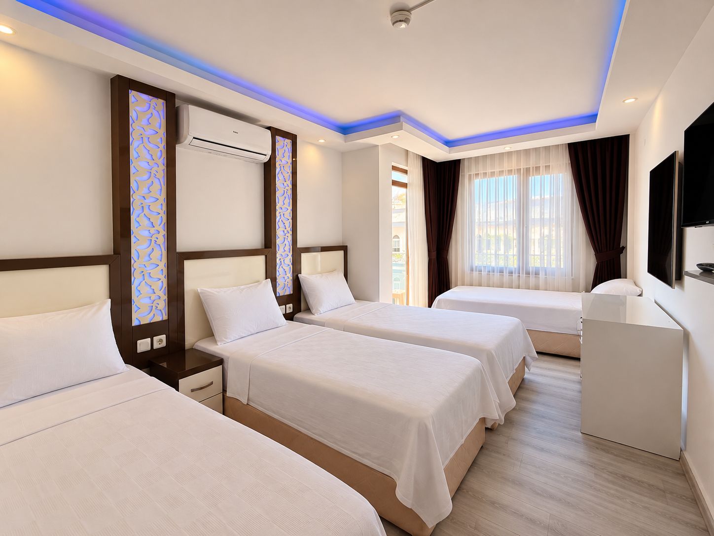 Quarto de hotel com três camas, televisão de tela plana e minibar.