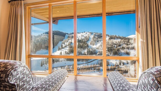 Quarto com uma janela grande que oferece vista para uma paisagem montanhosa coberta de neve.