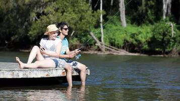 Duas pessoas pescam de um cais em um cenário natural.