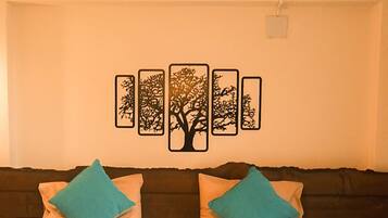 Uma cama bem arrumada com colcha verde-água, dois travesseiros azuis e uma toalha decorativa com uma flor vermelha.