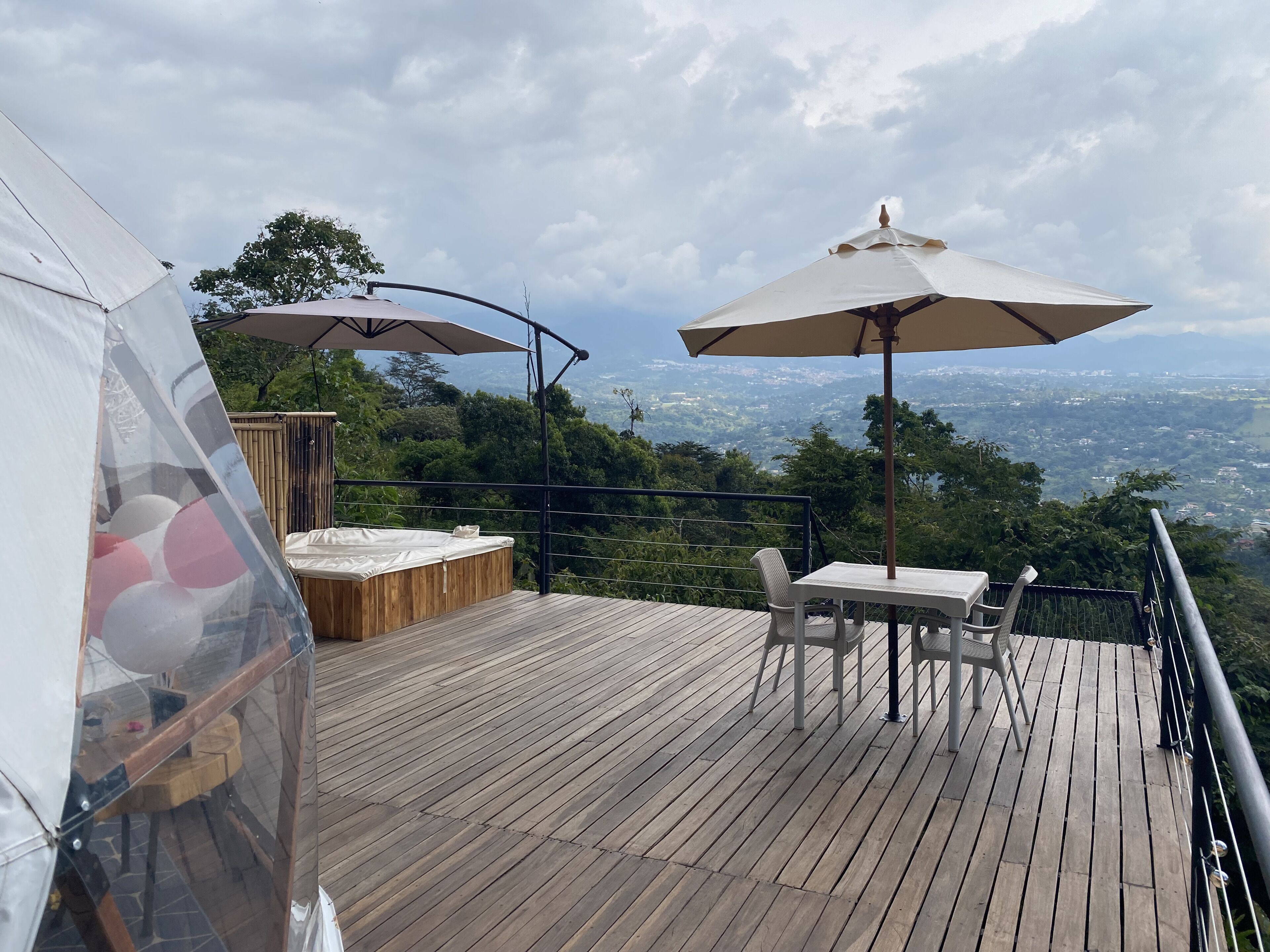 Um deck de madeira com uma banheira de hidromassagem, dois guarda-sóis e uma mesa com cadeiras.