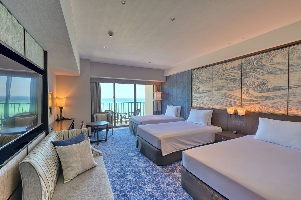 Quarto de hotel com duas camas, um sofá, uma varanda com vista e uma grande obra de arte na parede.