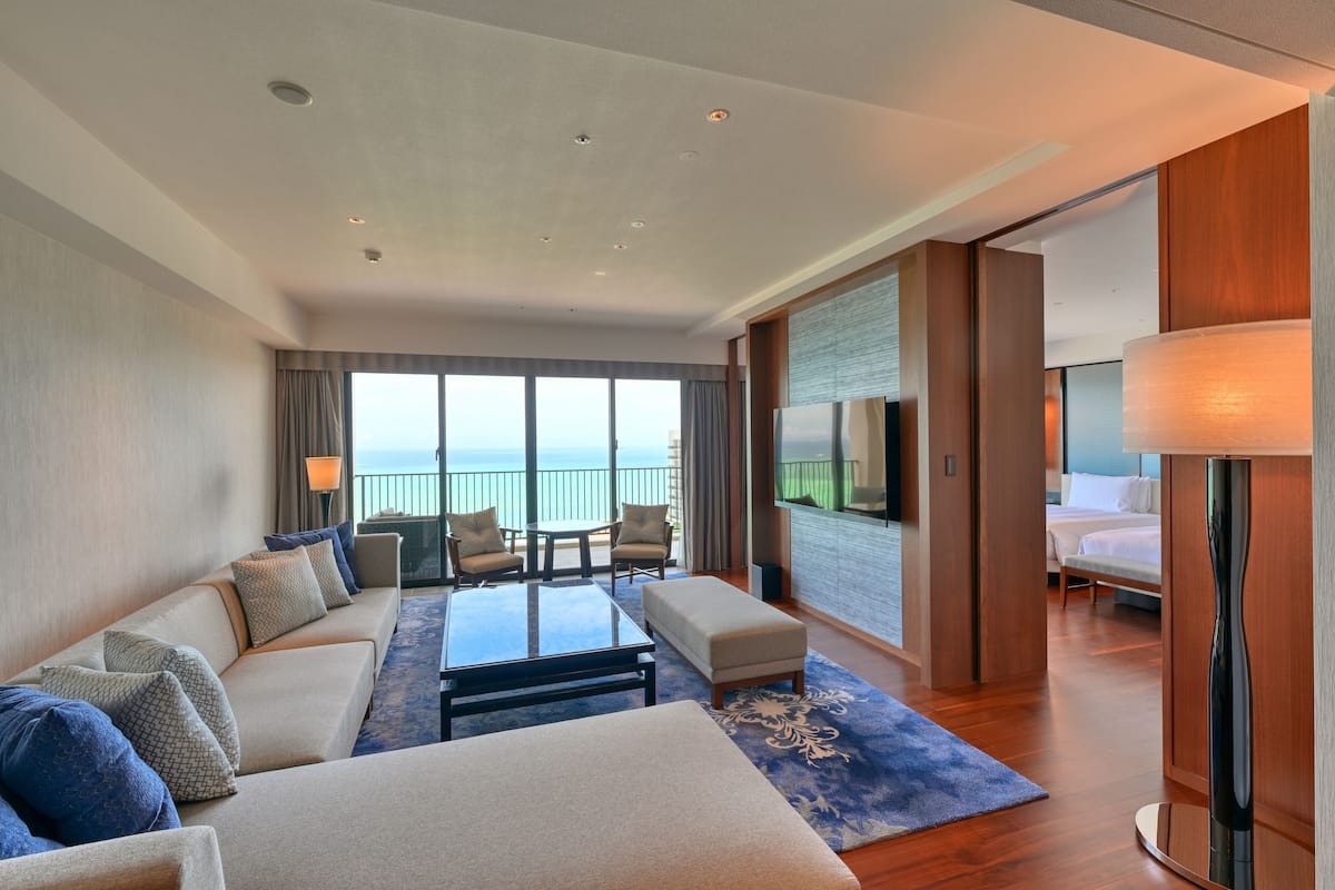 Quarto de hotel moderno com um sofá grande, uma mesa de centro e uma televisão. Possui uma varanda com vista para o mar.
