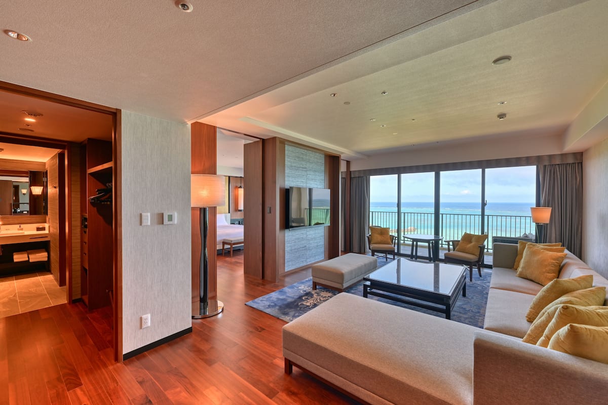 Quarto de hotel moderno com varanda, sofá, mesa de centro e vista para o mar.