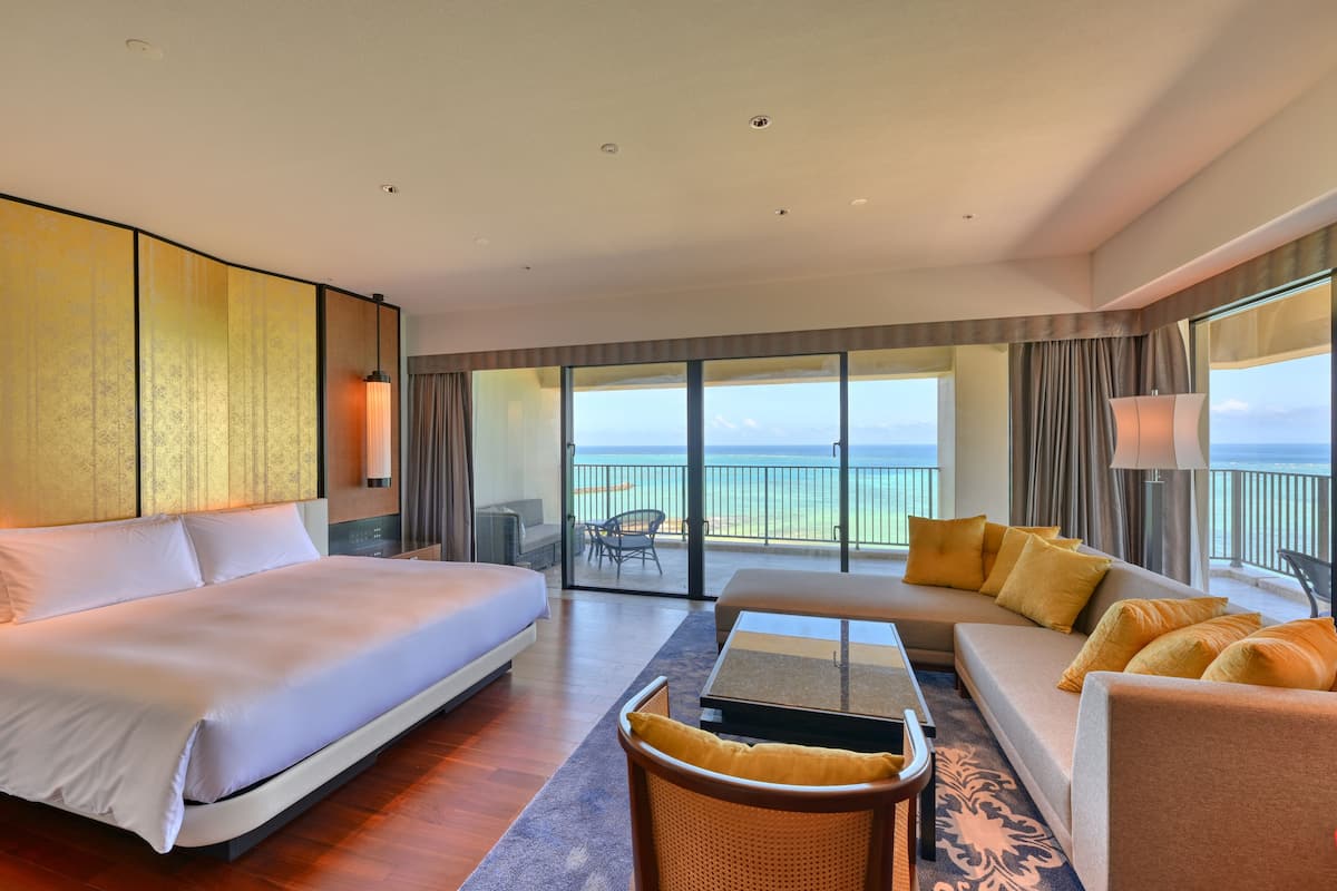Quarto de hotel com uma cama grande, um sofá, uma mesa pequena e vista para o oceano.