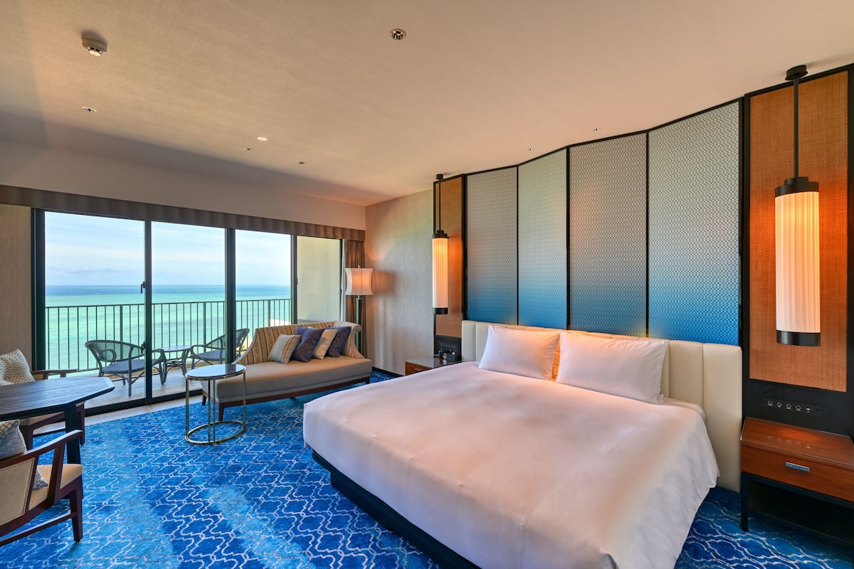 Quarto de hotel com uma cama grande, um sofá, uma mesa de jantar e vista para o oceano.