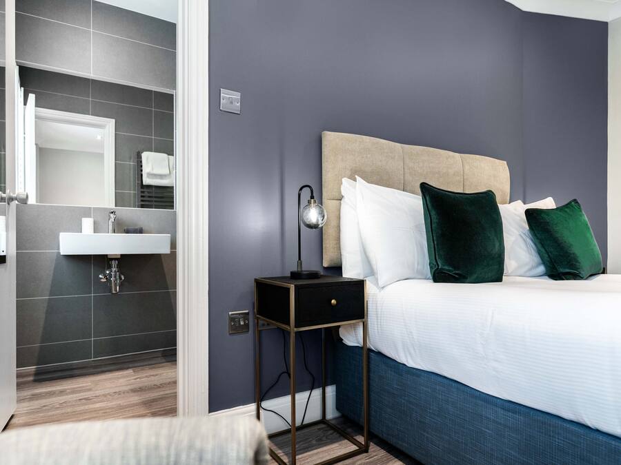 Quarto de hotel com cama, mesa de cabeceira e banheiro com pia e espelho.