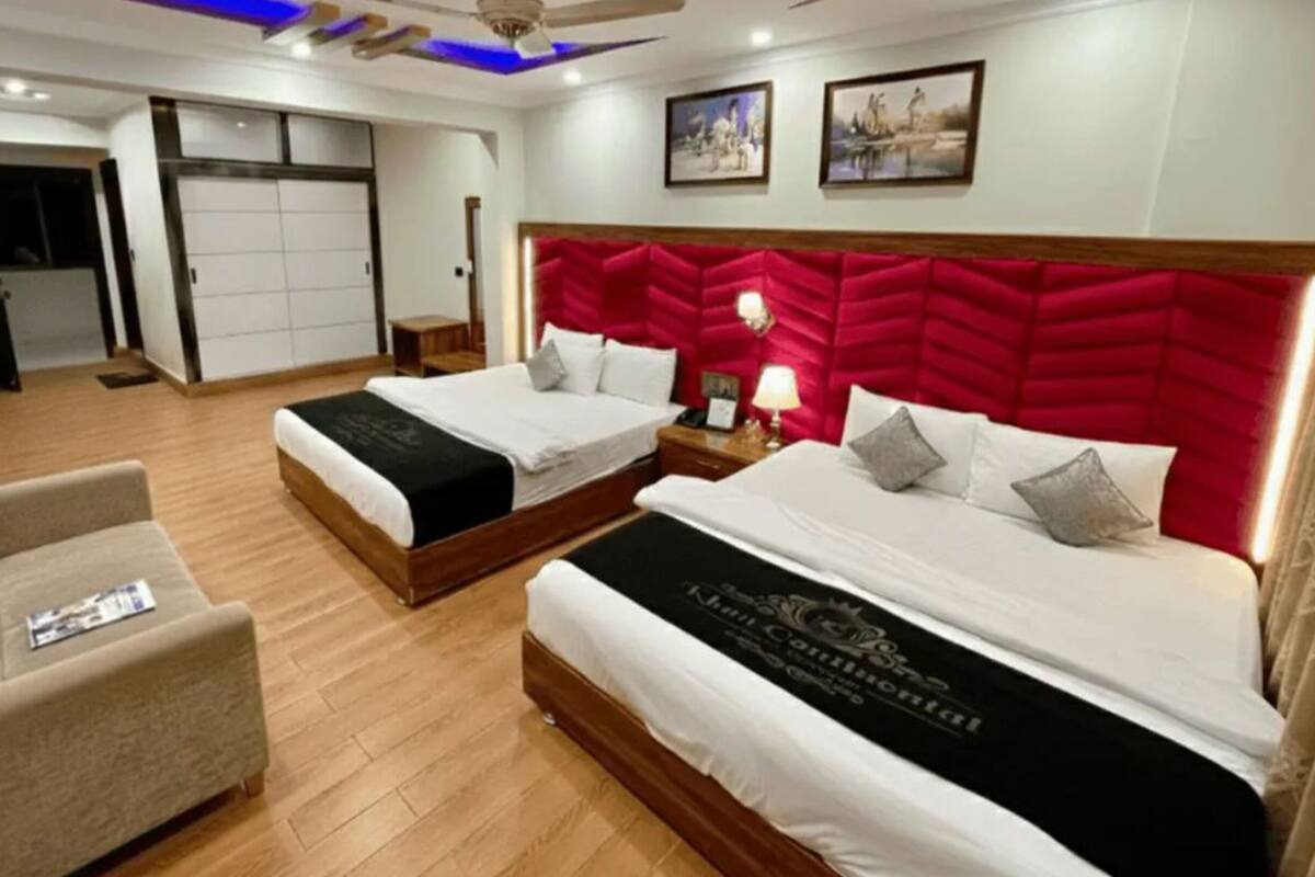 Quarto de hotel com duas camas, um sofá, um ventilador de teto e obras de arte nas paredes.