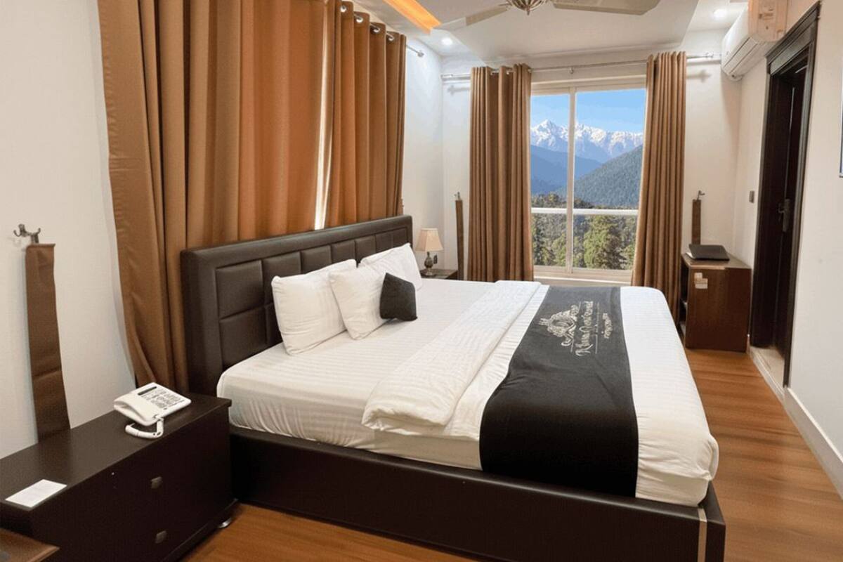 Quarto de hotel com uma cama grande, telefone de mesa, mesa de cabeceira e vista para as montanhas pela janela.