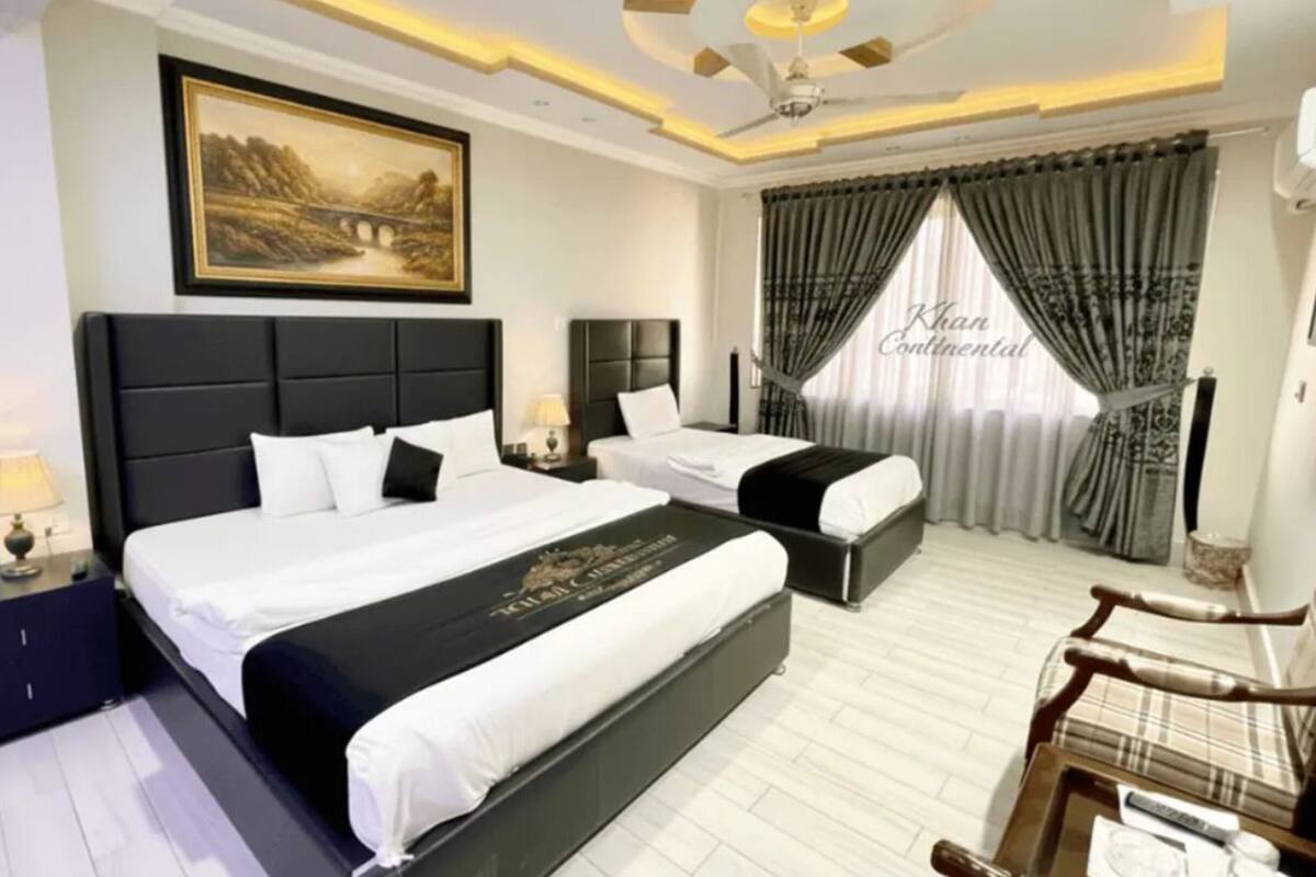 Quarto de hotel com duas camas, um quadro grande, um ventilador de teto e vista para o exterior.