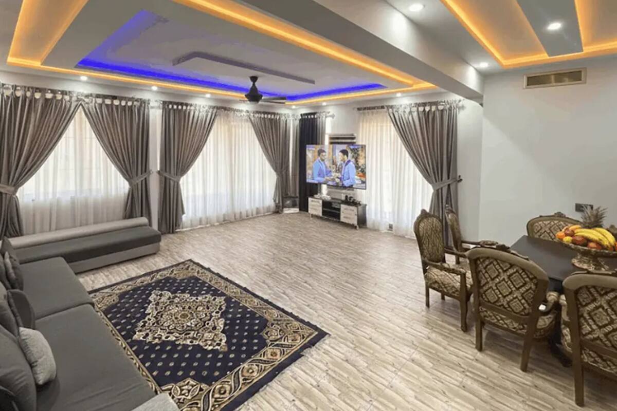 Uma sala de estar moderna com um sofá, uma mesa de jantar com cadeiras, uma televisão e um tapete estampado.