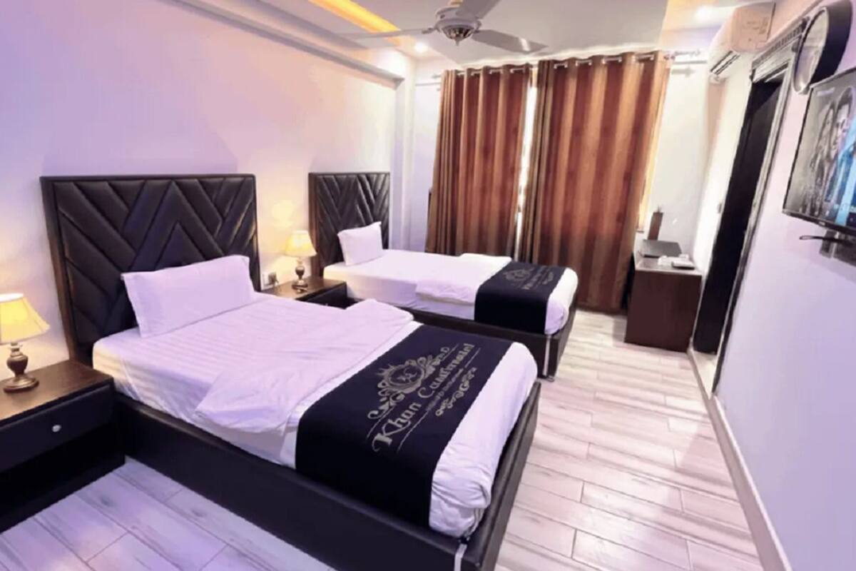 Quarto de hotel com duas camas, um ventilador de teto, televisão e janela com cortinas.