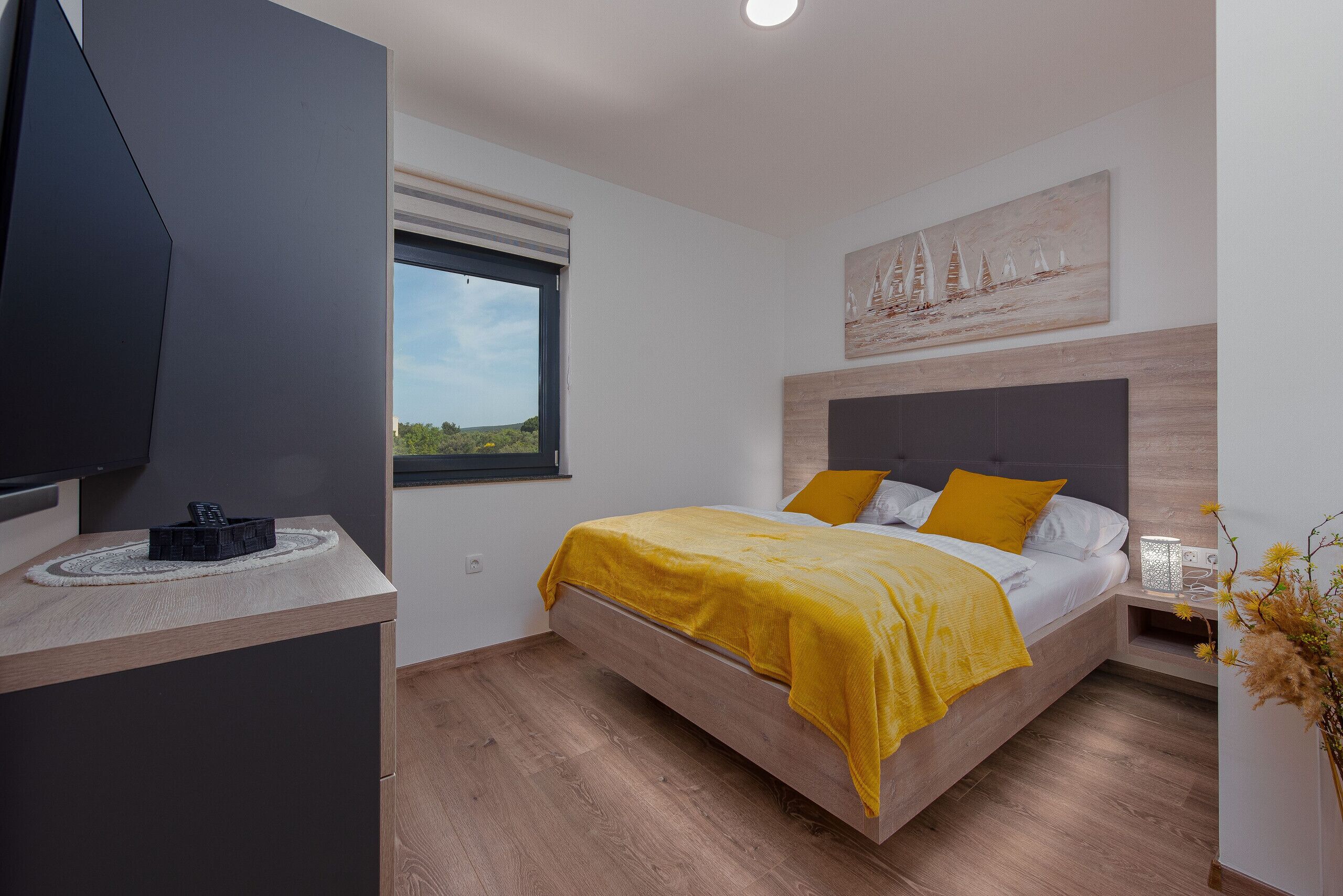 Quarto moderno com cama, mesa de cabeceira, televisão e janela com vista.