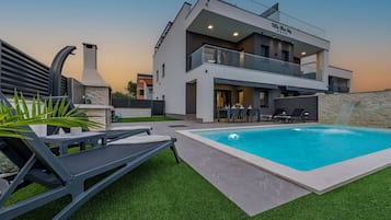 Uma casa moderna de dois andares com piscina, área de estar externa e um muro de pedra.