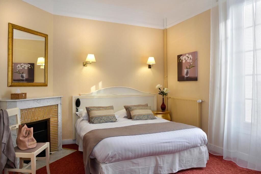 Quarto de hotel com cama grande, lareira, espelho, luminárias de parede e um quadro.