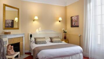Quarto de hotel com cama grande, lareira, espelho, luminárias de parede e um quadro.