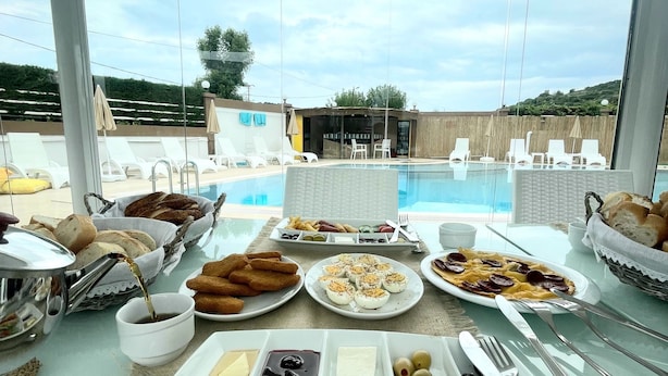 Mesa de jantar com diversos pratos e vista para uma piscina e espreguiçadeiras.