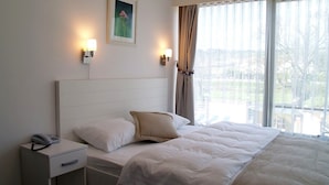 Quarto de hotel com uma cama, uma mesa de cabeceira com telefone e duas luminárias fixadas na parede.