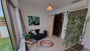Uma sala de estar moderna com um sofá preto, um armário de madeira, um lustre e uma janela grande.