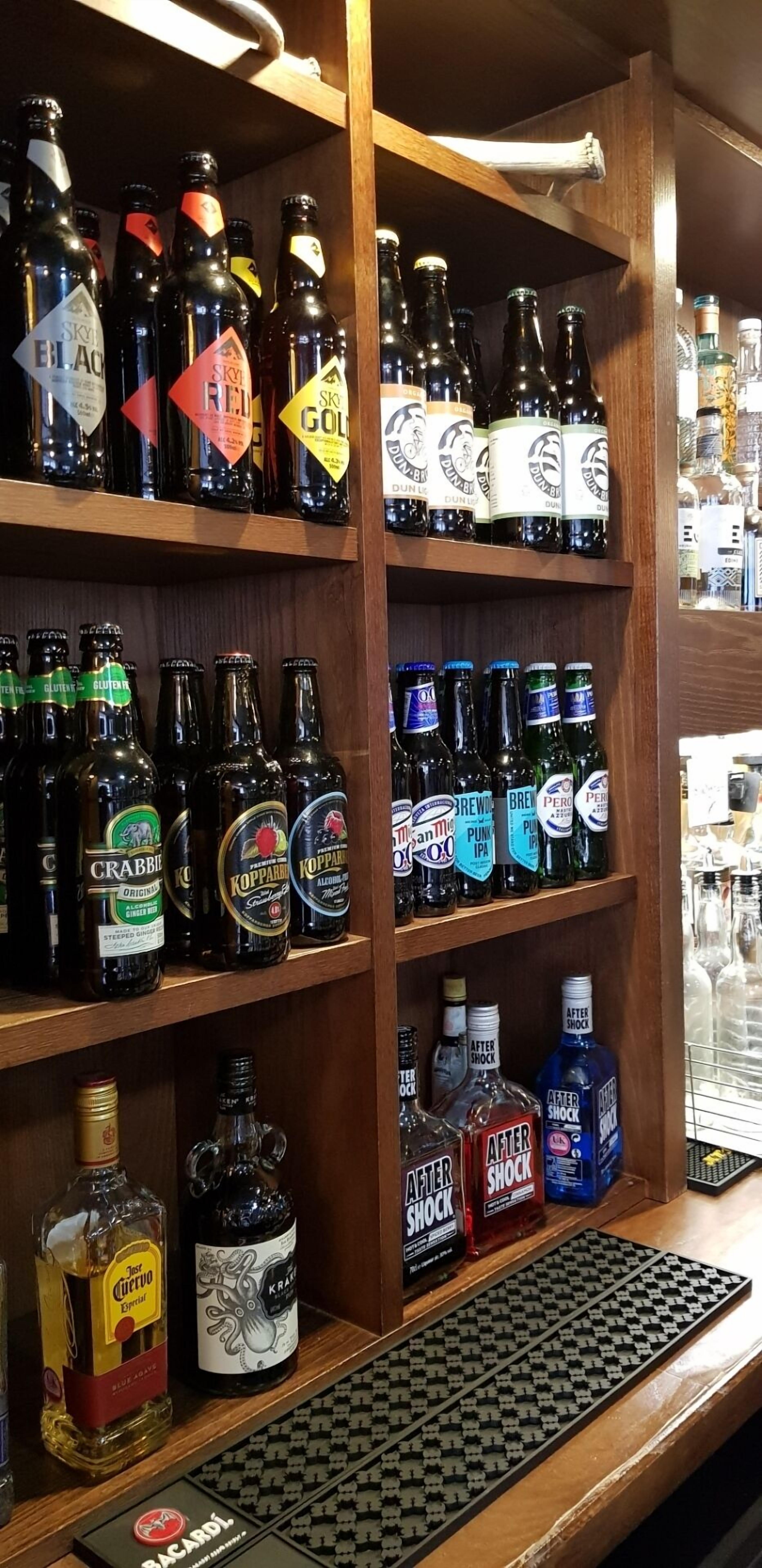 Estante repleta de garrafas de bebidas alcoólicas diversas, incluindo marcas como Sky Black, Sky Gold e After Shock.