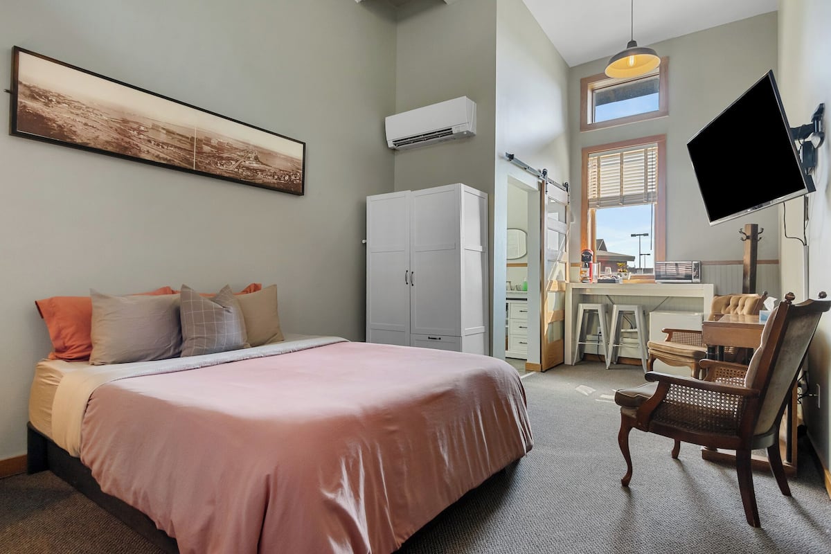 Quarto com cama, guarda-roupa, ar condicionado, escrivaninha, cadeira e televisão.