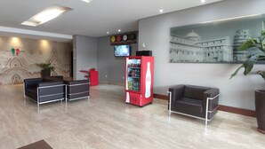 Um saguão de hotel com balcão de recepção, área de estar, refrigerador de Coca-Cola e uma pintura grande de um edifício famoso.