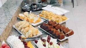 Buffet com diversos alimentos, incluindo frutas, doces e pão.