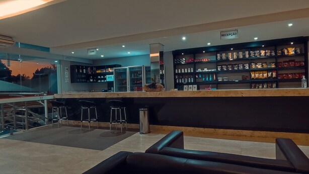 Uma área de bar moderna com assentos, balcão de recepção e prateleiras repletas de lanches e bebidas.