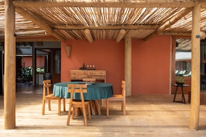 Uma área de jantar de madeira com mesa, cadeiras, um armário de madeira e uma estrutura de telhado de palha.
