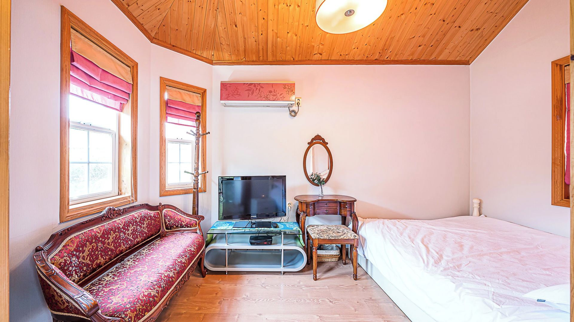 Quarto com teto de madeira, uma cama, televisão, sofá e cômoda.