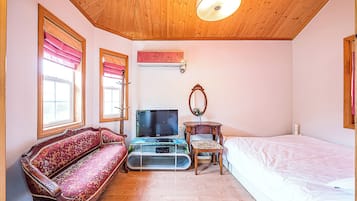Quarto com teto de madeira, uma cama, televisão, sofá e cômoda.
