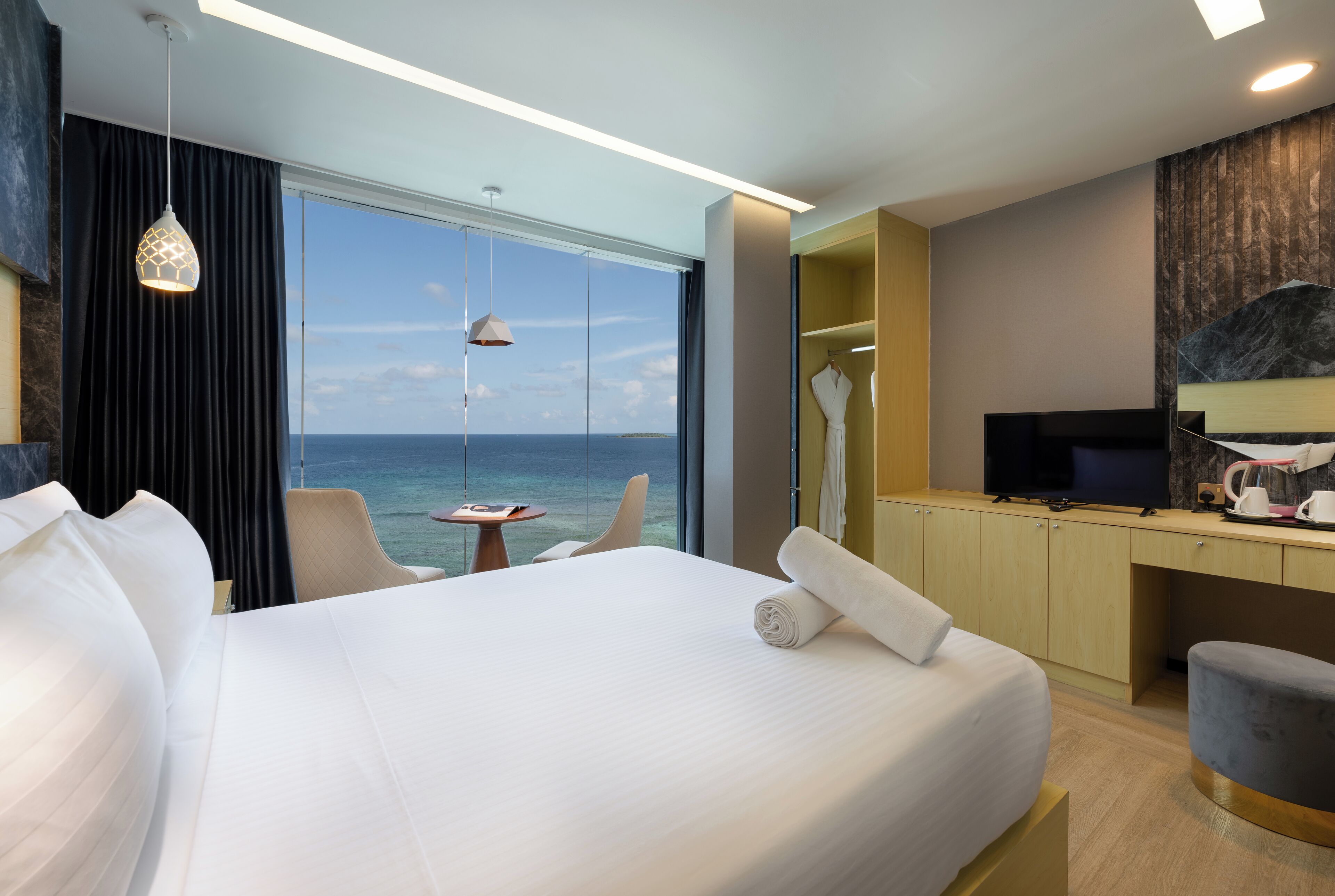 Quarto de hotel moderno com uma cama grande, uma escrivaninha, uma televisão e vista para o oceano.