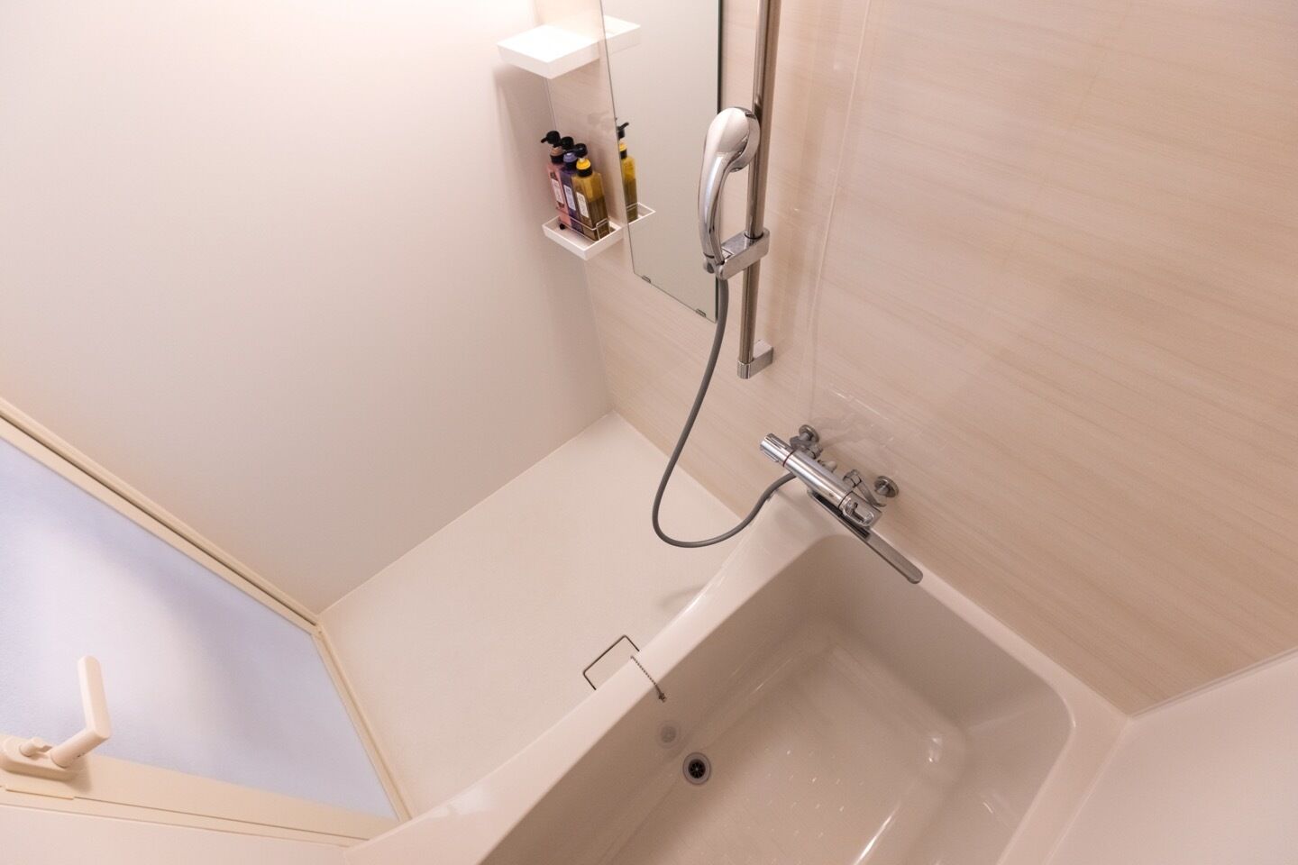 Casa de banho com banheira, chuveiro manual e prateleira com artigos de higiene pessoal.