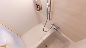 Casa de banho com banheira, chuveiro manual e prateleira com artigos de higiene pessoal.