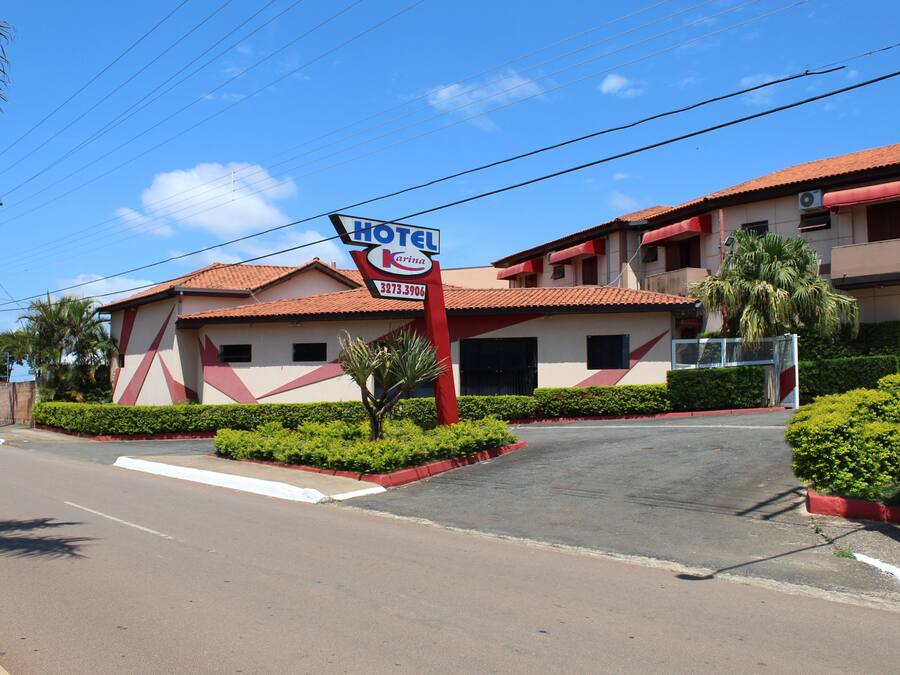 Um hotel com fachada vermelha e branca, uma placa de identificação visível e uma área de jardim bem cuidada.