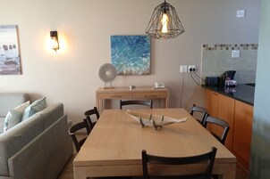 Uma sala de jantar com uma mesa de madeira, cadeiras, um ventilador, uma luminária na parede e um quadro.