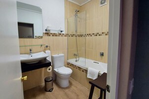 Casa de banho com sanita, lavatório e zona de duche com cabine de vidro.