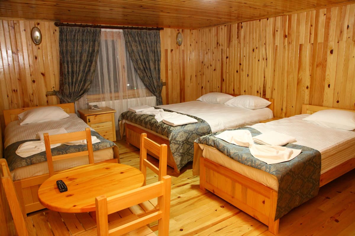 Quarto de cabana de madeira com três camas, uma mesa de madeira e uma cadeira.