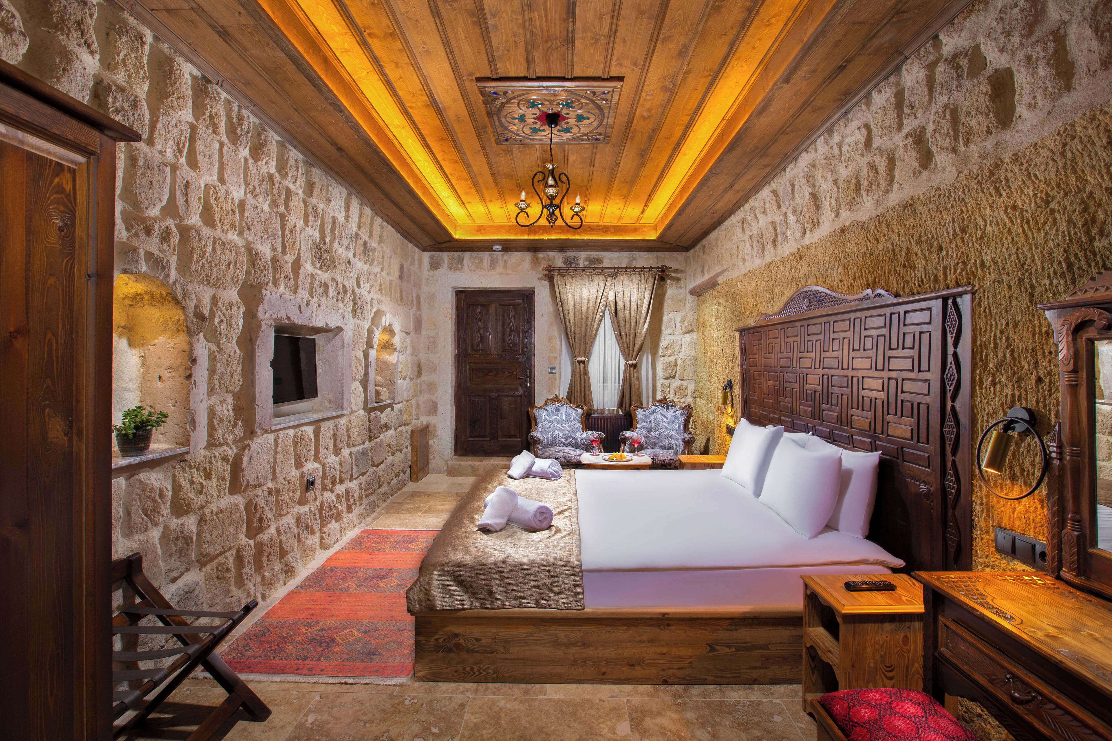 Quarto tradicional com paredes de pedra, uma cama de madeira, uma mesa pequena e um banco.