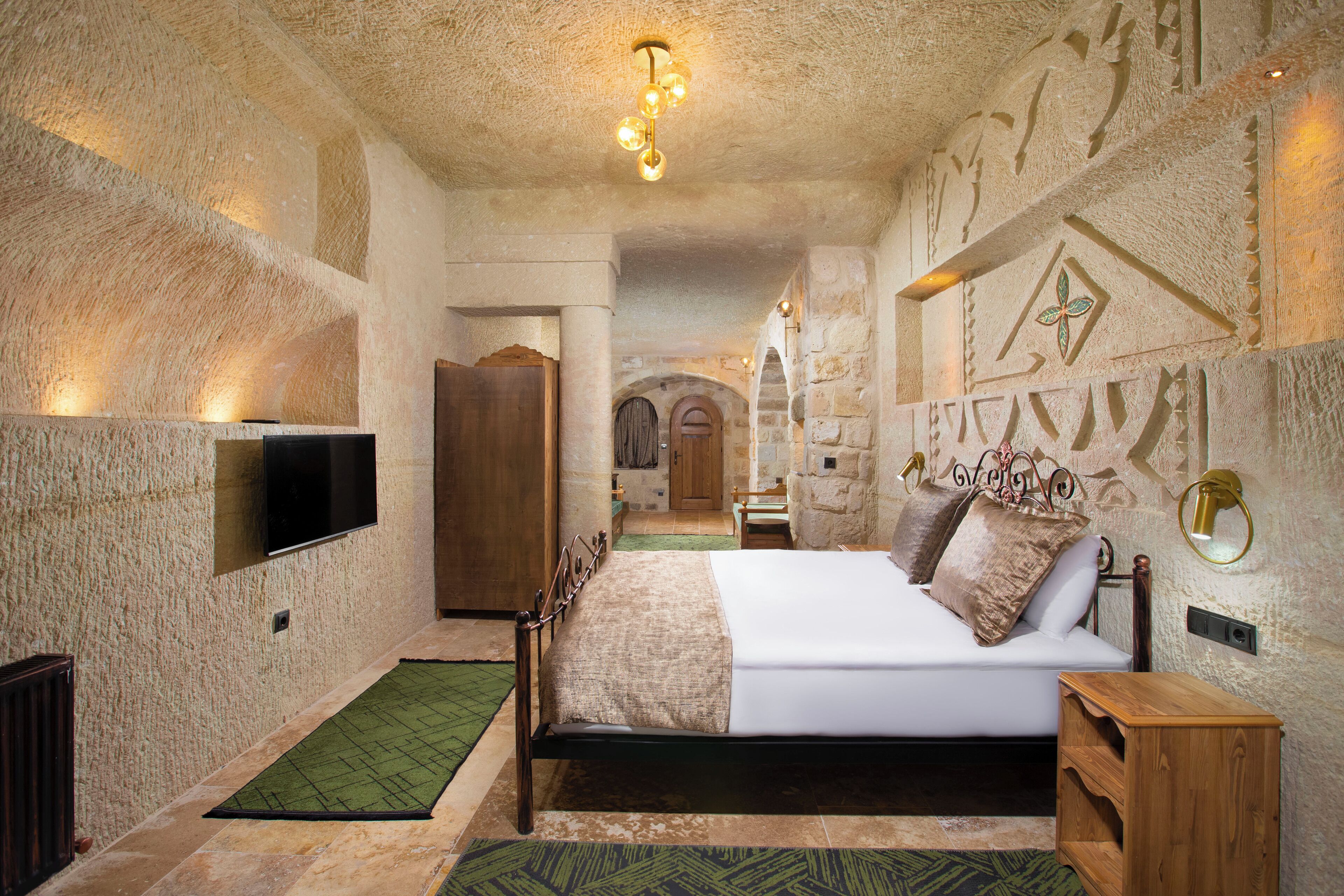 Quarto com cama, mesa de cabeceira de madeira, televisão de tela plana na parede e tapete verde no chão.