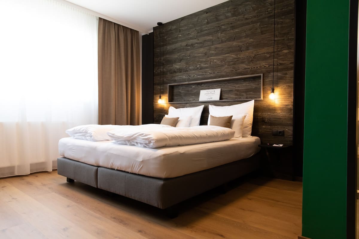 Quarto de hotel moderno com uma cama grande, cabeceira de madeira e uma parede verde.