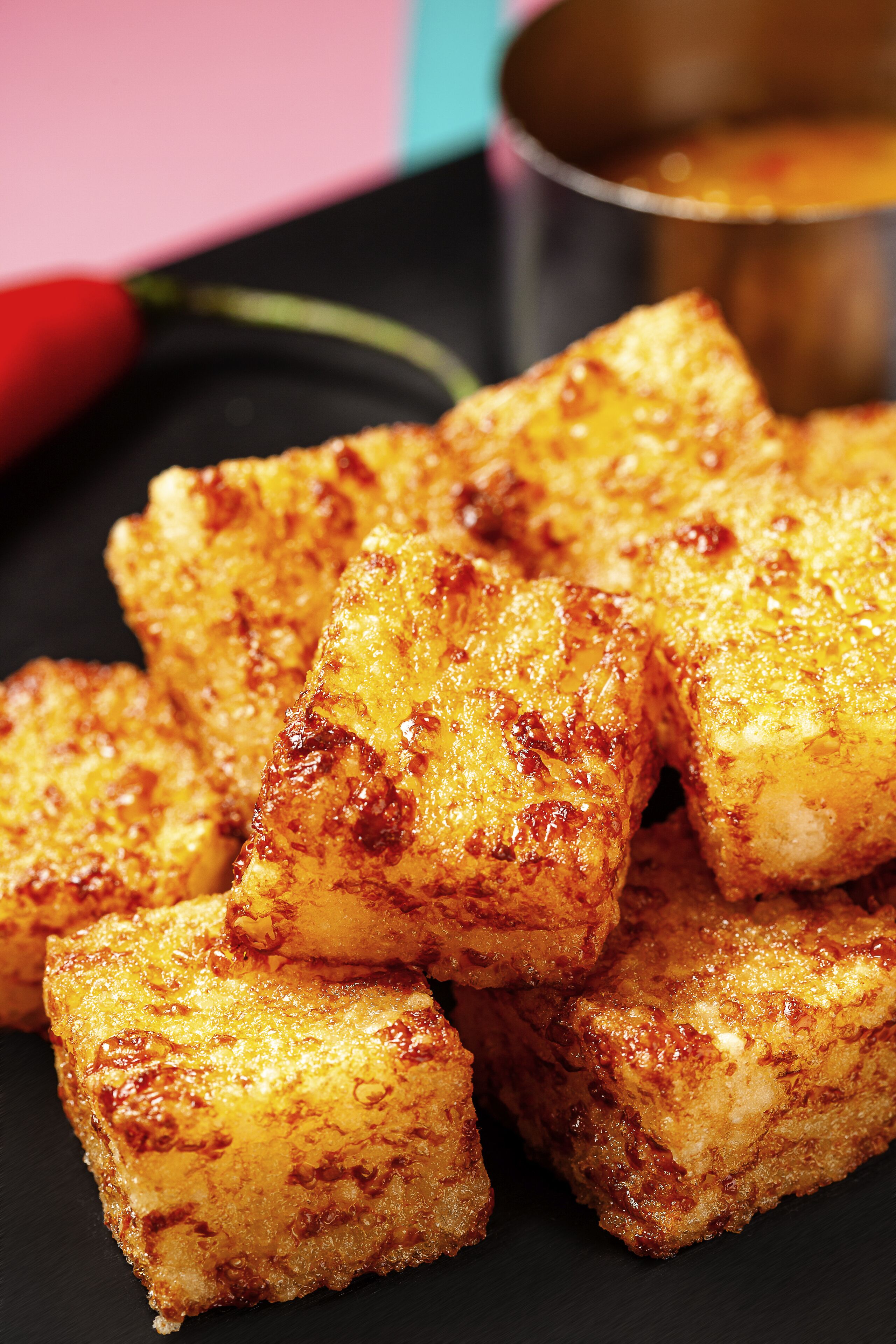 Close-up de alimentos fritos, dourados e com aparência de tofu, sobre um prato escuro.