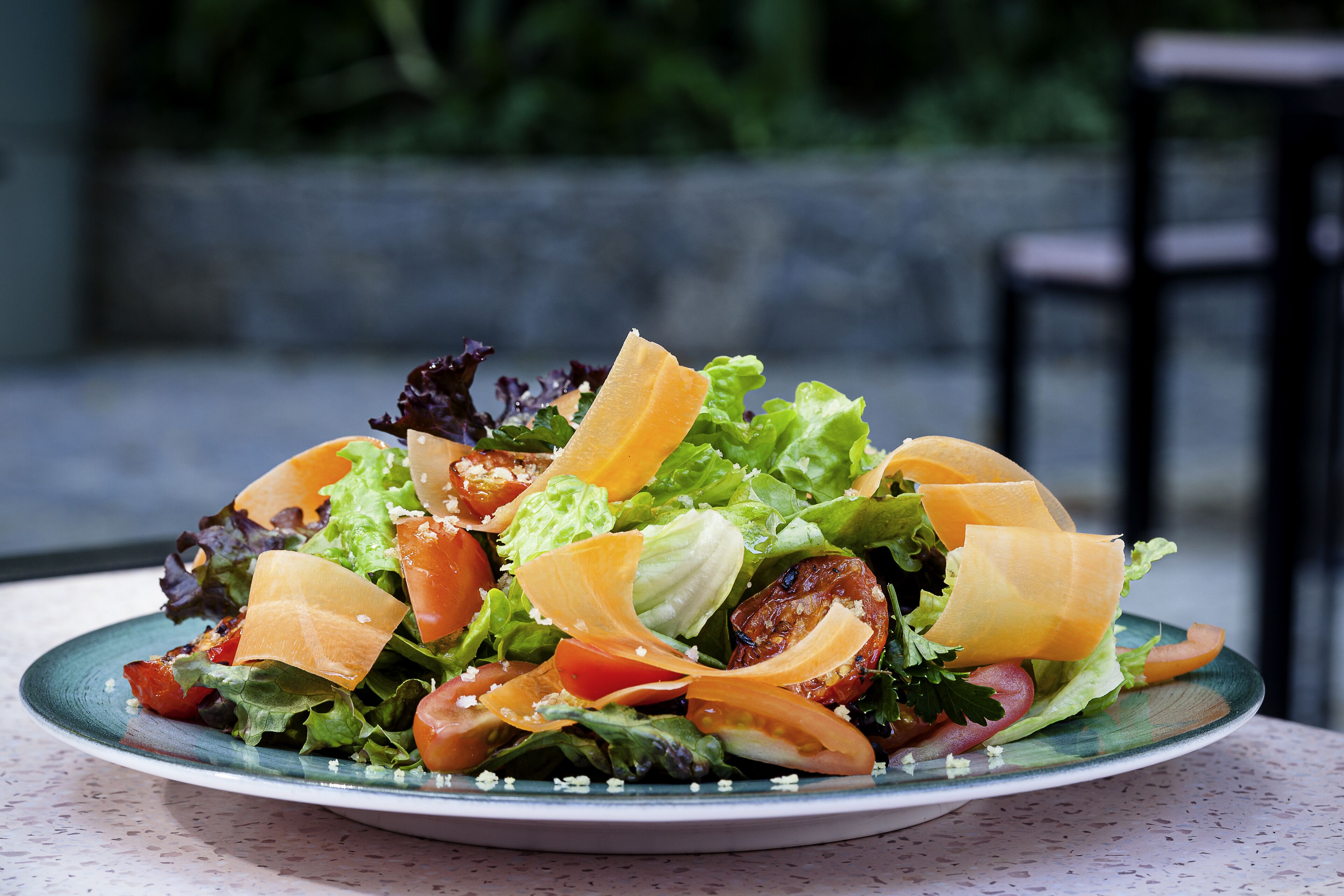 Uma salada de folhas verdes variadas com tomates e queijo sobre uma mesa.