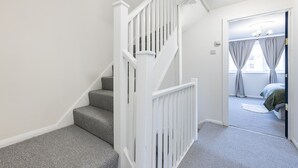 Uma escadaria com corrimãos brancos leva a um quarto com cama e cortinas.