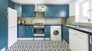 Cozinha compacta com armários verde-água, geladeira branca, forno embutido, máquina de lavar e piso estampado.