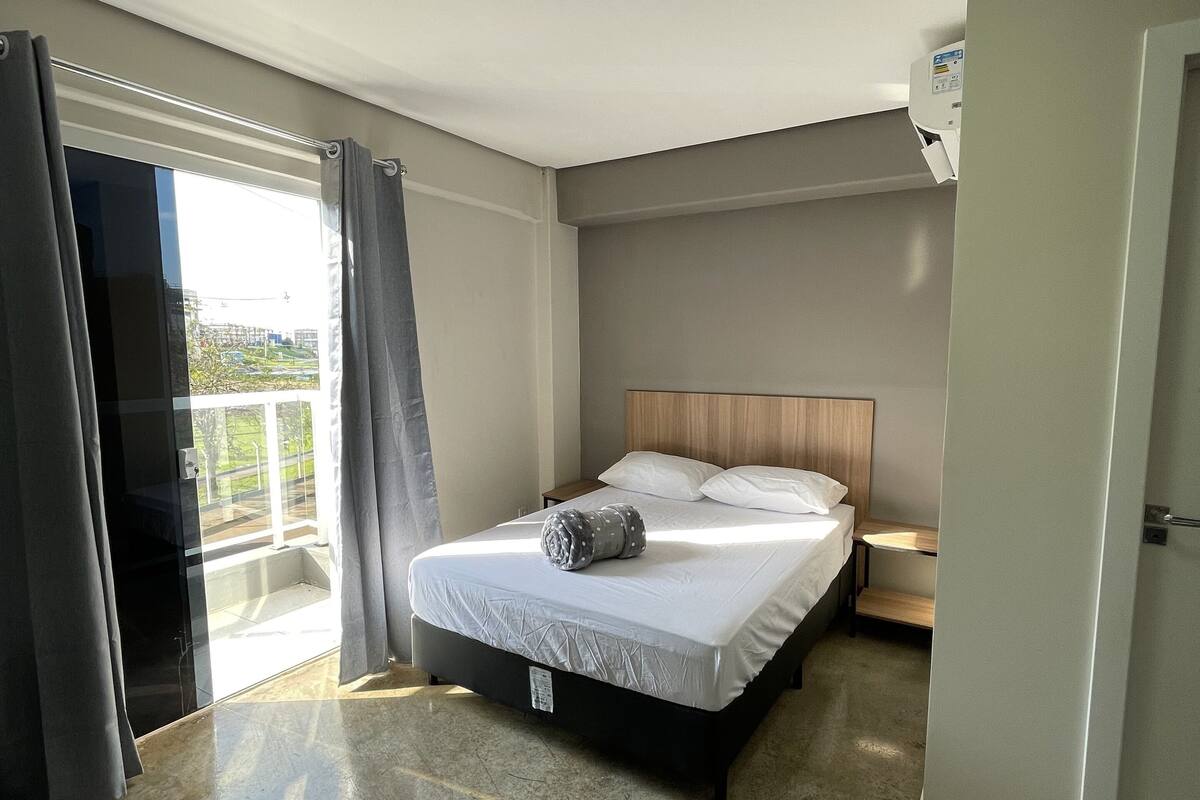 Quarto de hotel moderno com uma cama grande, vista para o exterior e um ventilador de teto.