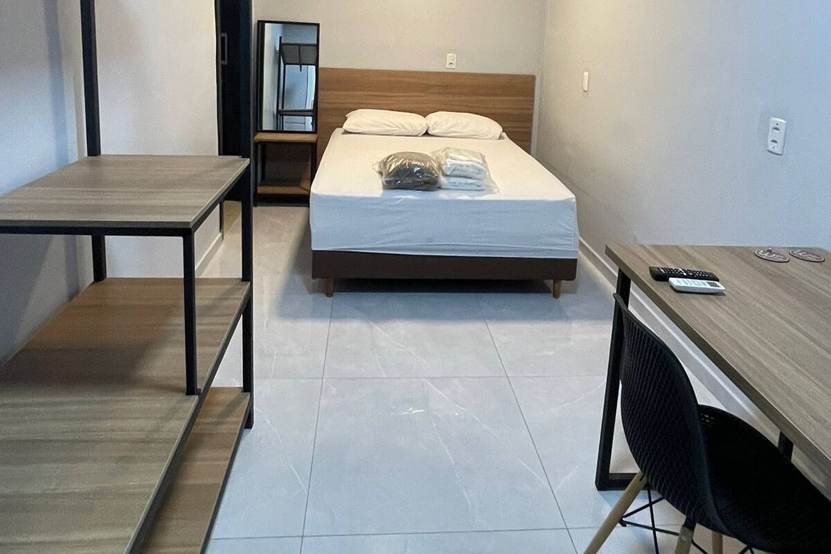 Quarto compacto com uma cama, uma escrivaninha e uma mesinha.